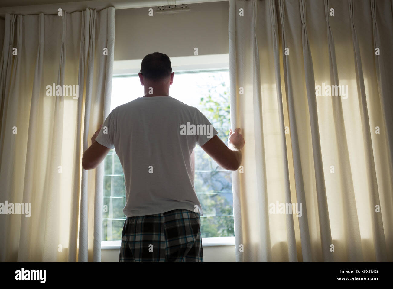 Rear view of man opening window curtain in bedroom Stock Photo - Alamy