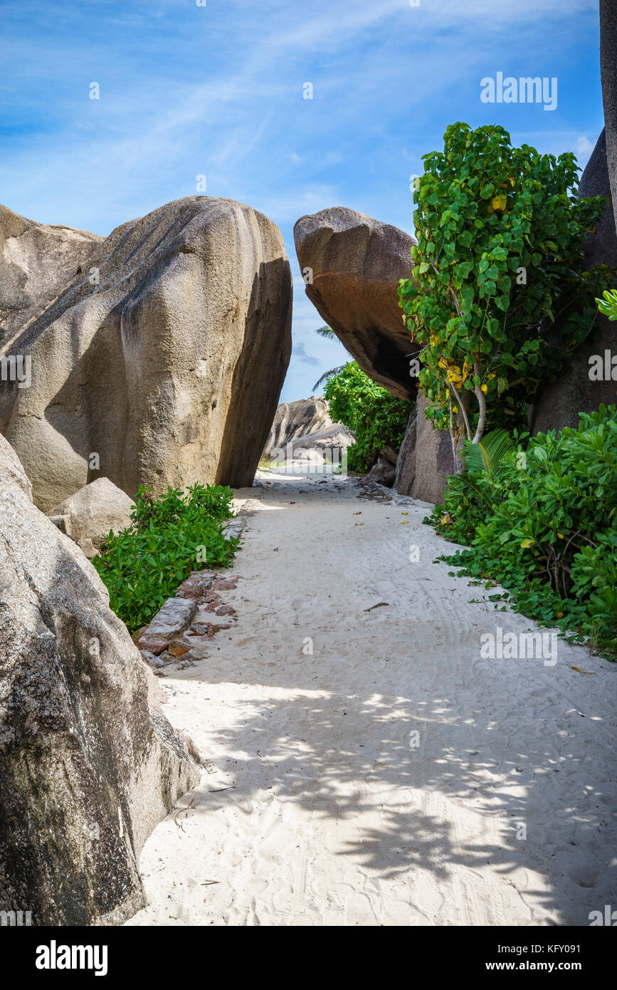 walking a footpath through a granite arch to the beach at anse source d ...