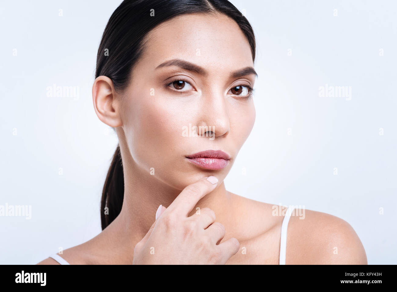 Dark-haired woman posing while touching chin with finger Stock Photo ...