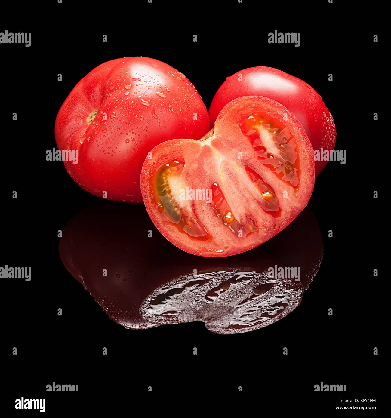 Two red whole and one half-cut tomato closeup isolated on black glossy ...