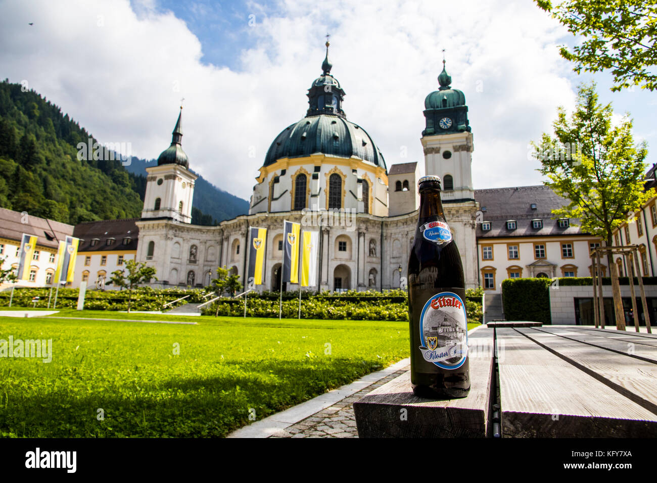 A bottle of Ettaler beer in front of the main facade of of Ettal Abbey ...