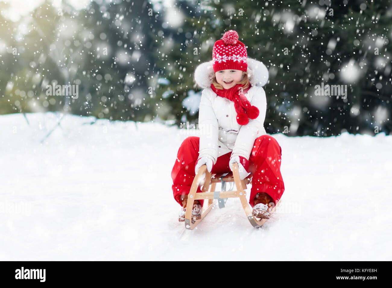Little girl enjoying a sleigh ride. Child sledding. Toddler kid riding a sledge. Children play ...