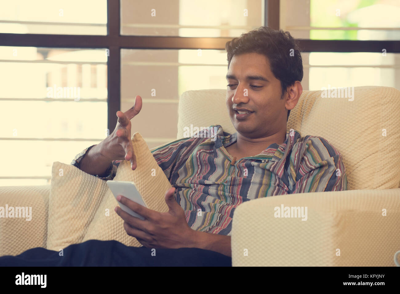 indian male using phone on sofa Stock Photo - Alamy