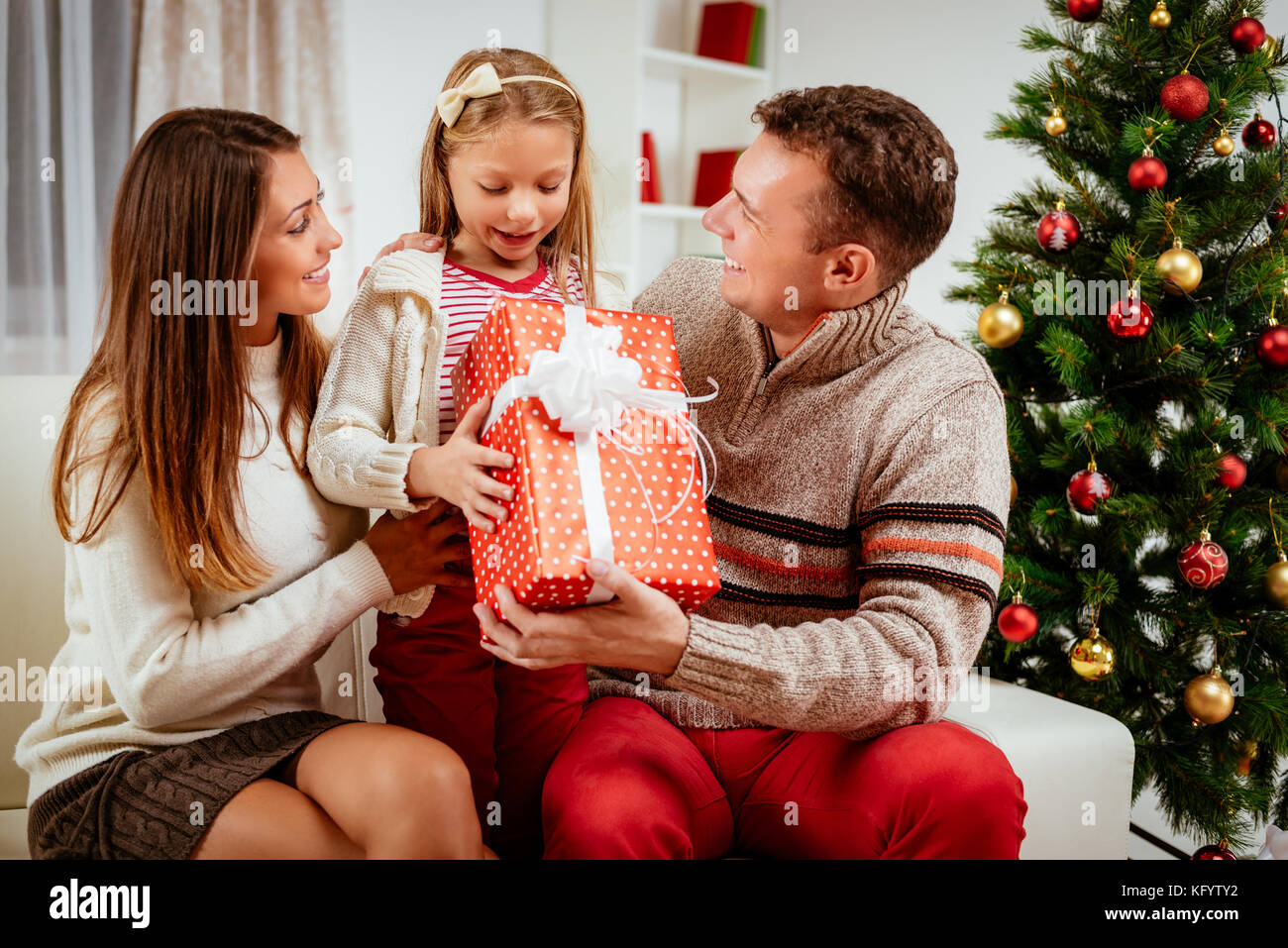 Beautiful young smiling parents give a present to their cute happy ...