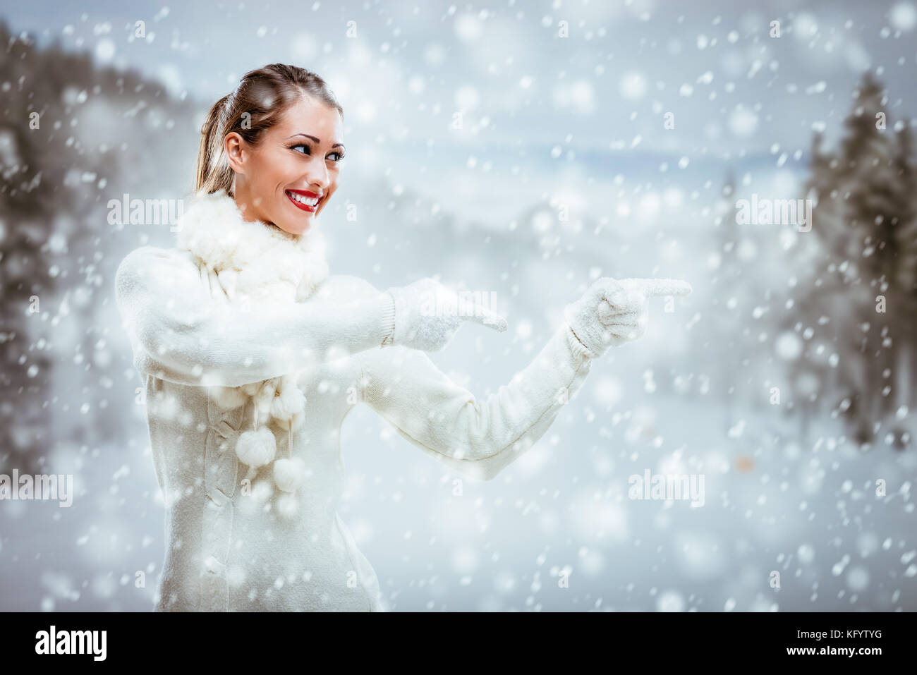 Beautiful young woman in white winter clothes at snow pointing to ...