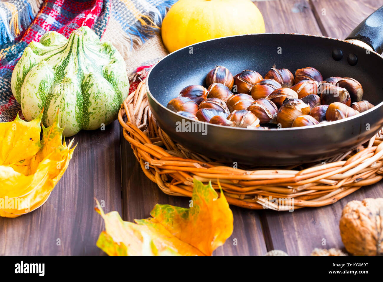 Roasted chestnuts in a pan with autumn pumpkins and dried maple leaves ...