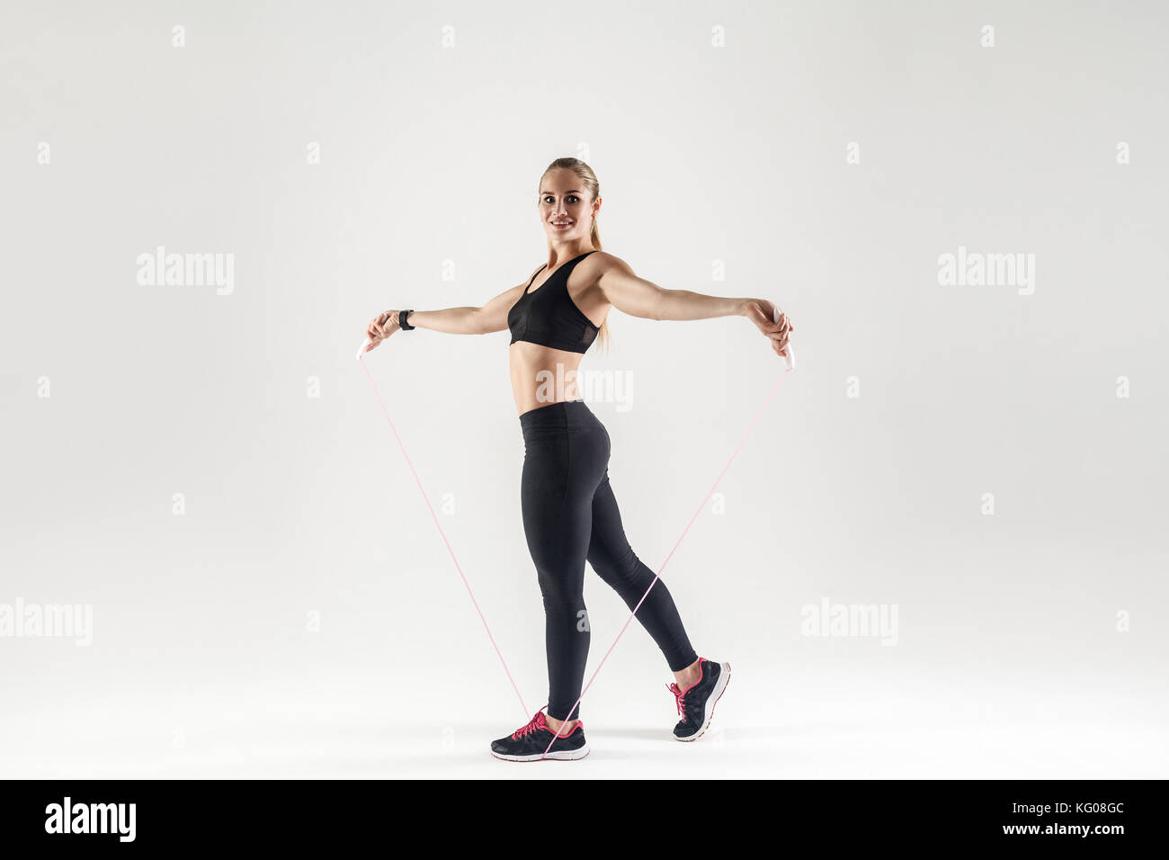 Happy beautiful blonde woman, holding skipping rope and toothy smiling ...