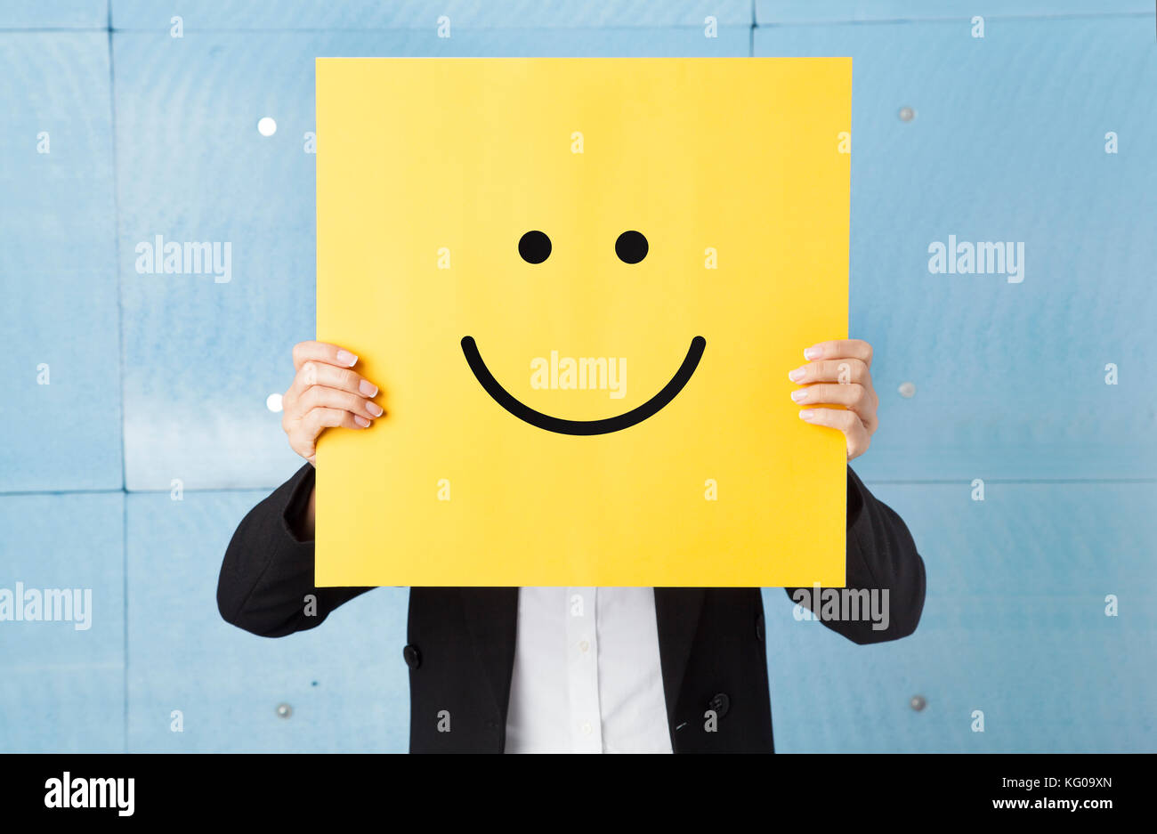 Young woman hiding her face with a yellow paper with a smiley face on ...