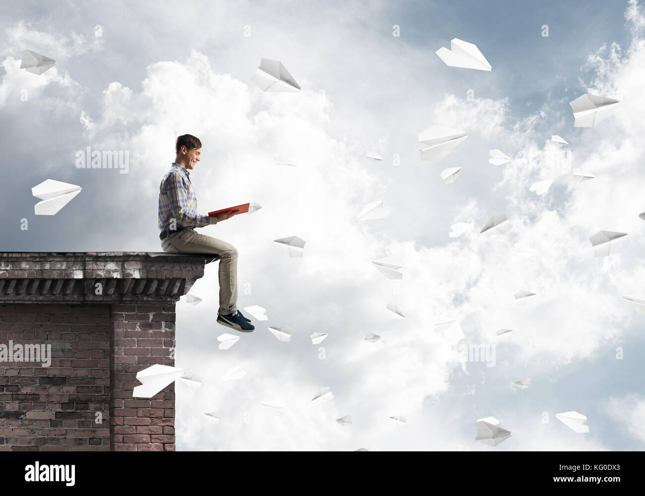 Handsome student guy on roof edge reading book and paper planes fly ...