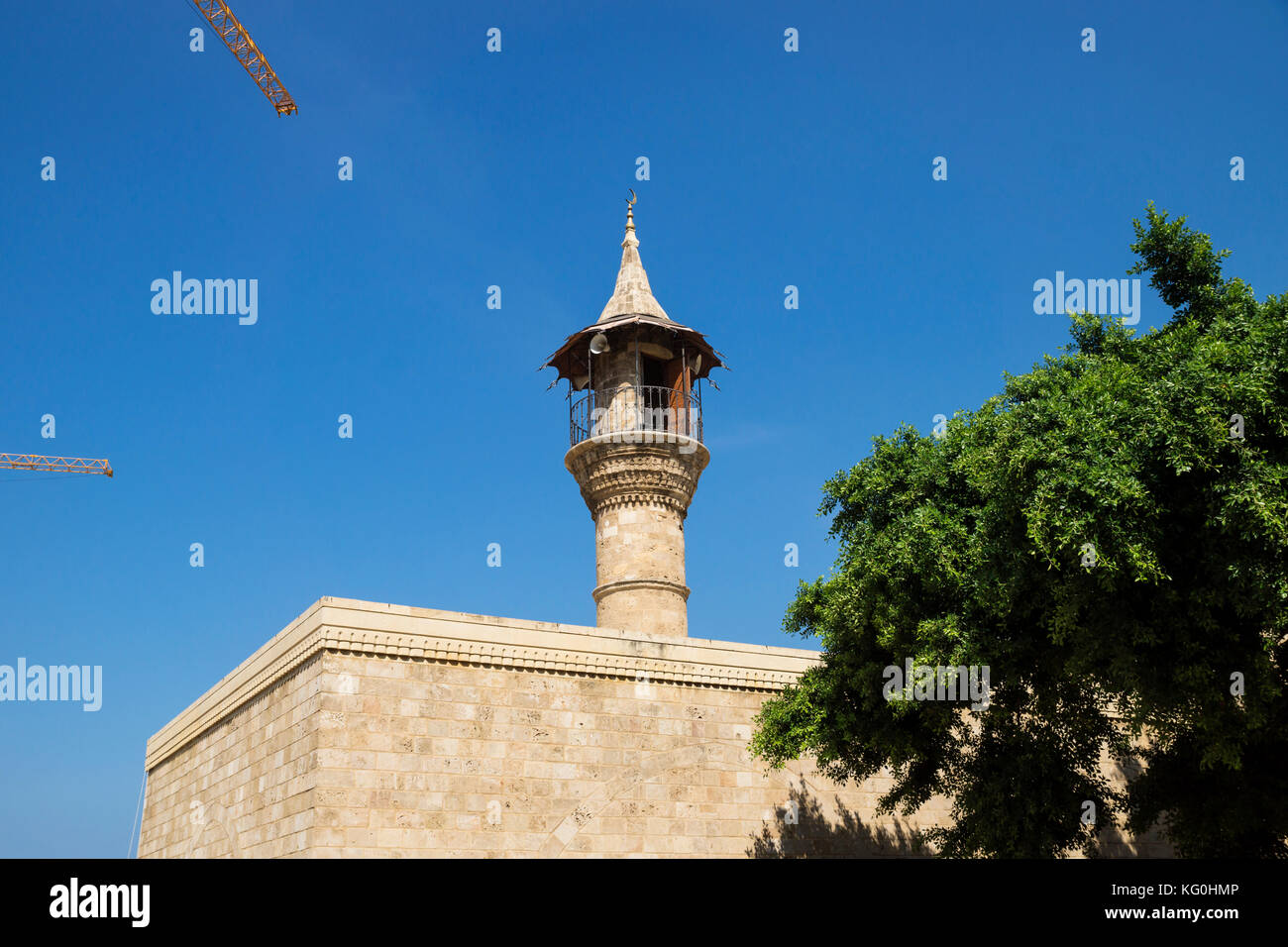 Minarette of Mosque, a green tree and cranes on a blue sky in the city ...