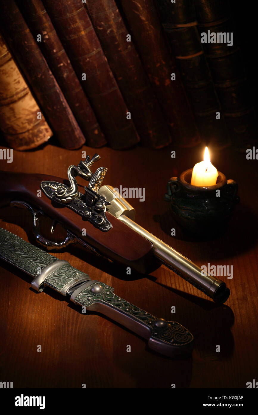 Lighting candle near ancient pistol and dagger on wooden surface with ...