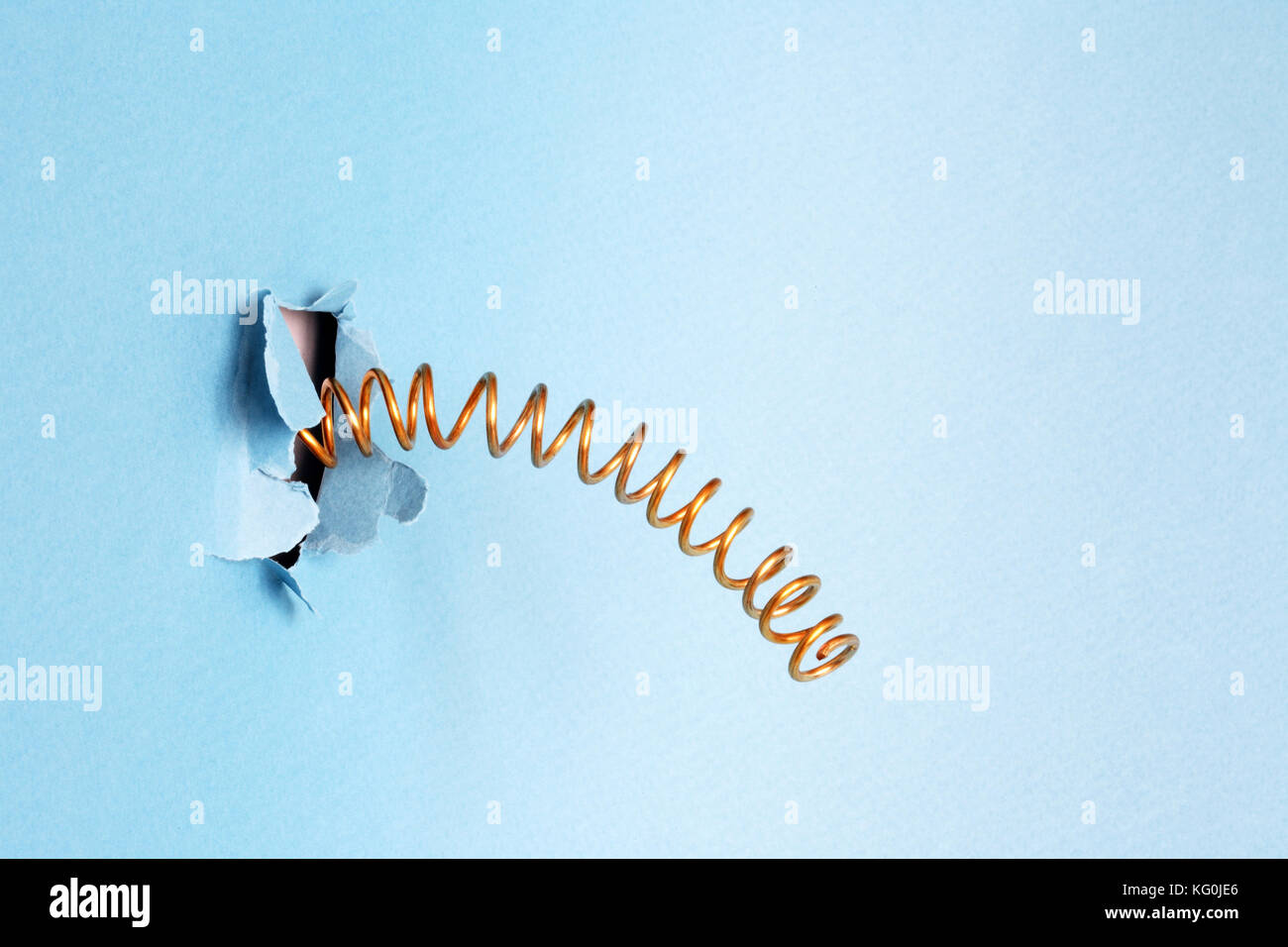 Metal spring jump out through a blue disrupt paper background Stock ...