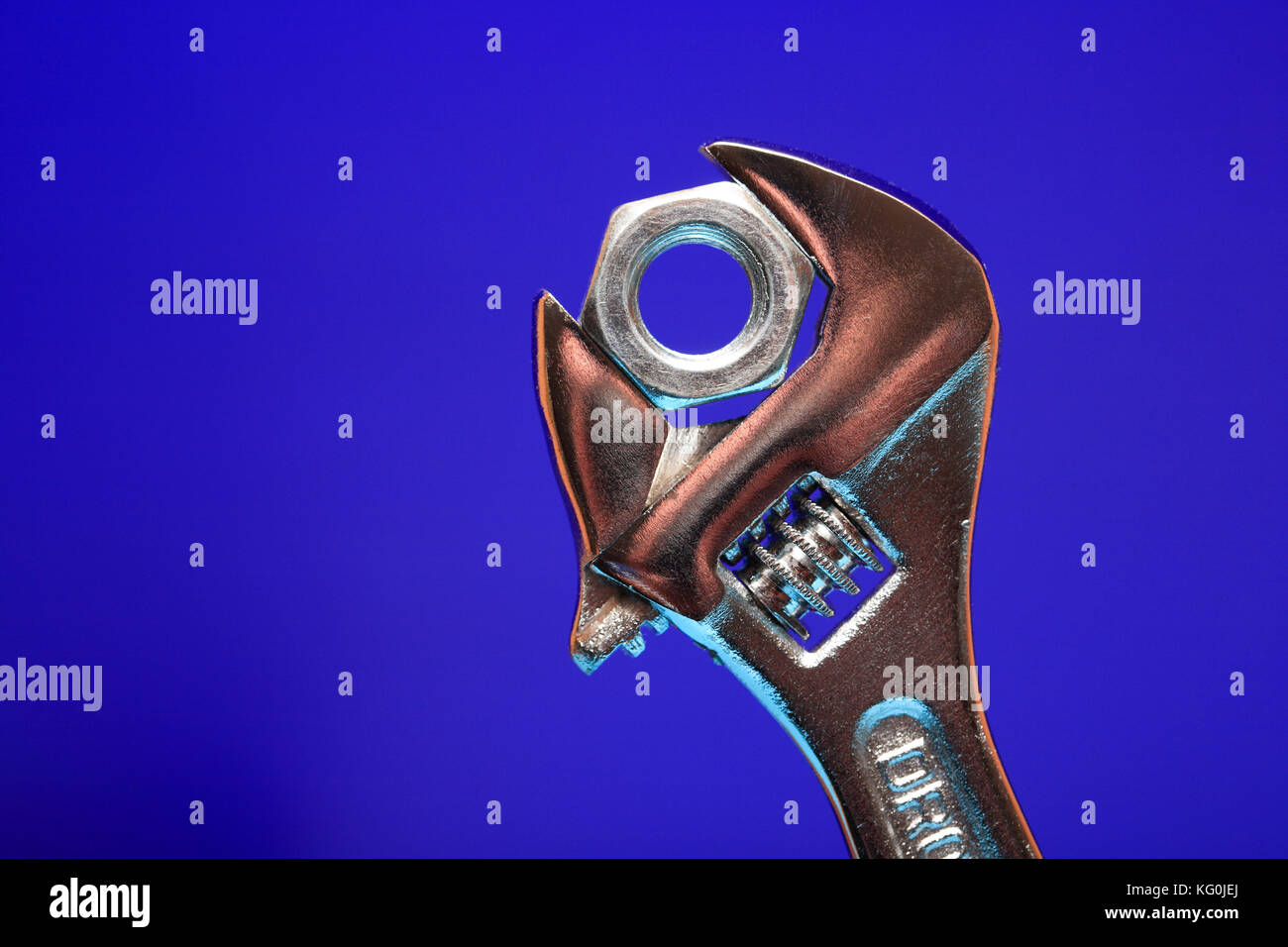 Extreme closeup of adjustable wrench gripping a screw nut on blue ...
