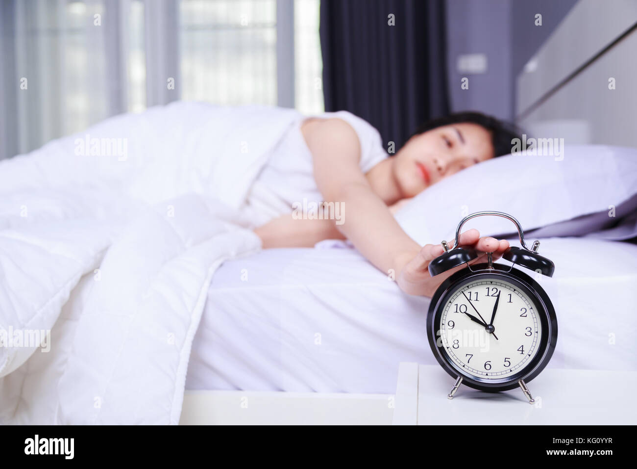 Woman Sleeping On Bed And Rise Hand To Turn Off Alarm Clock In The