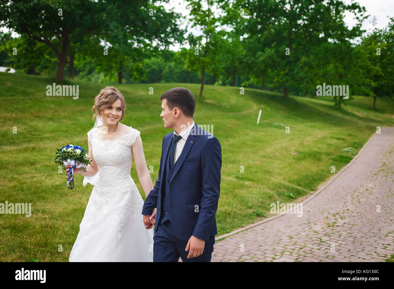 Beautiful bride and handsome groom smiling and walking holding hands in ...