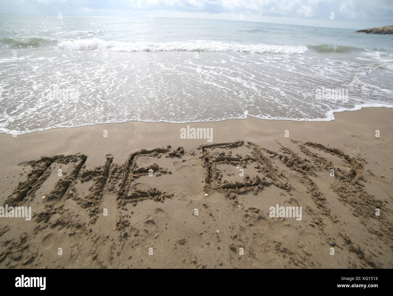 word THE END written on the sand and the wave that is deleting the text ...