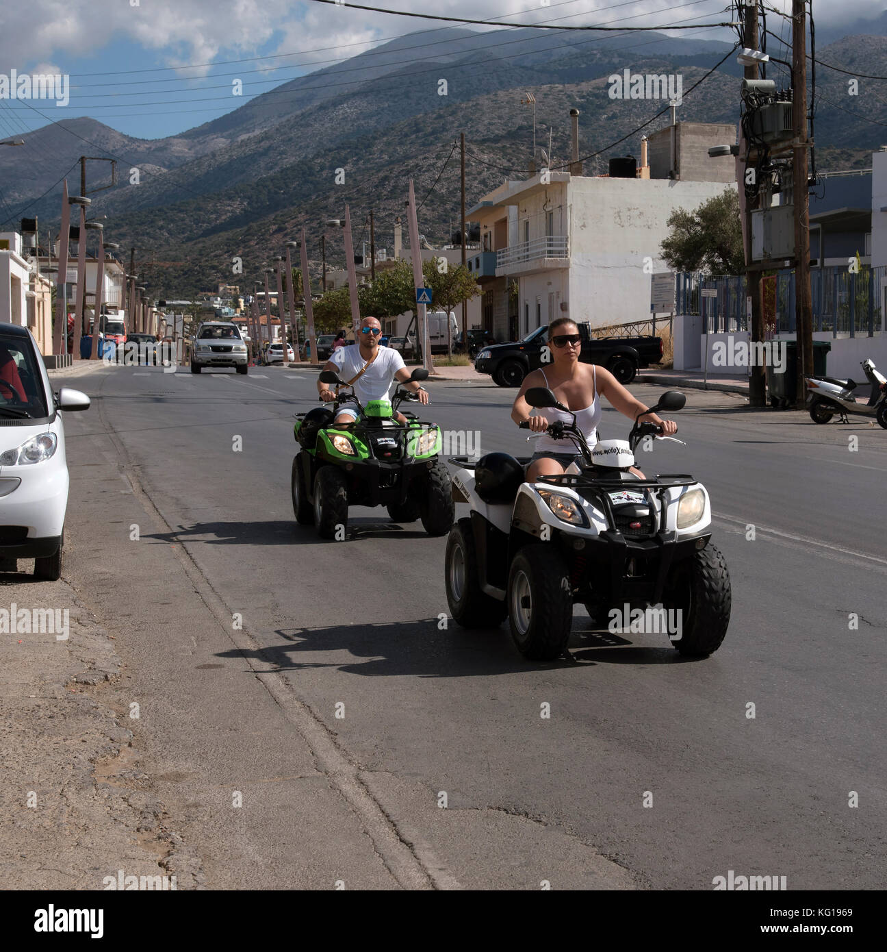 Couple riding quad bikes through Malia town centre, Crete, Greece ...