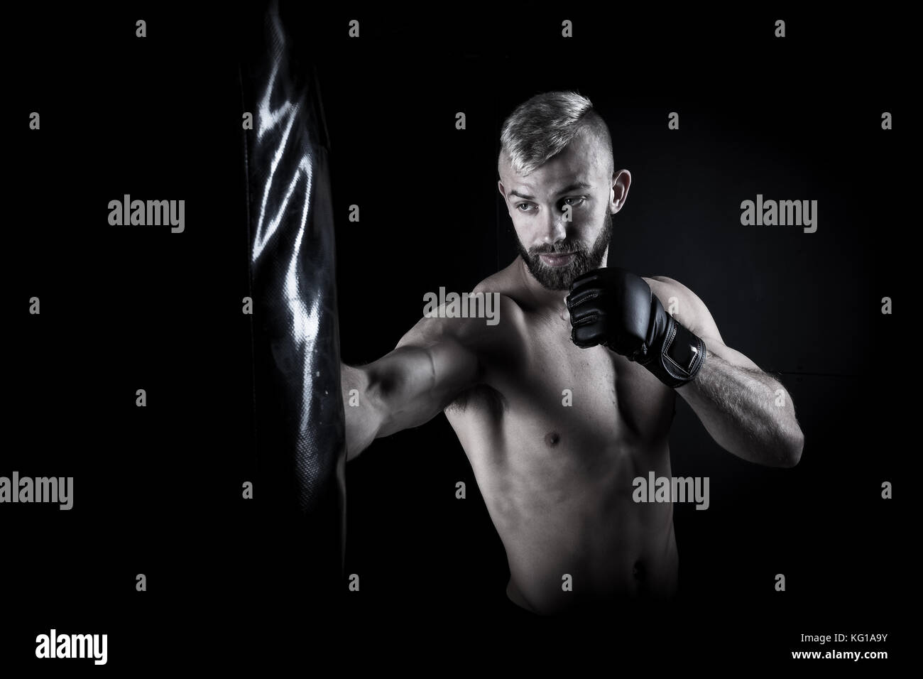 Male Athlete boxer punching a punching bag with dramatic edgy lighty in ...