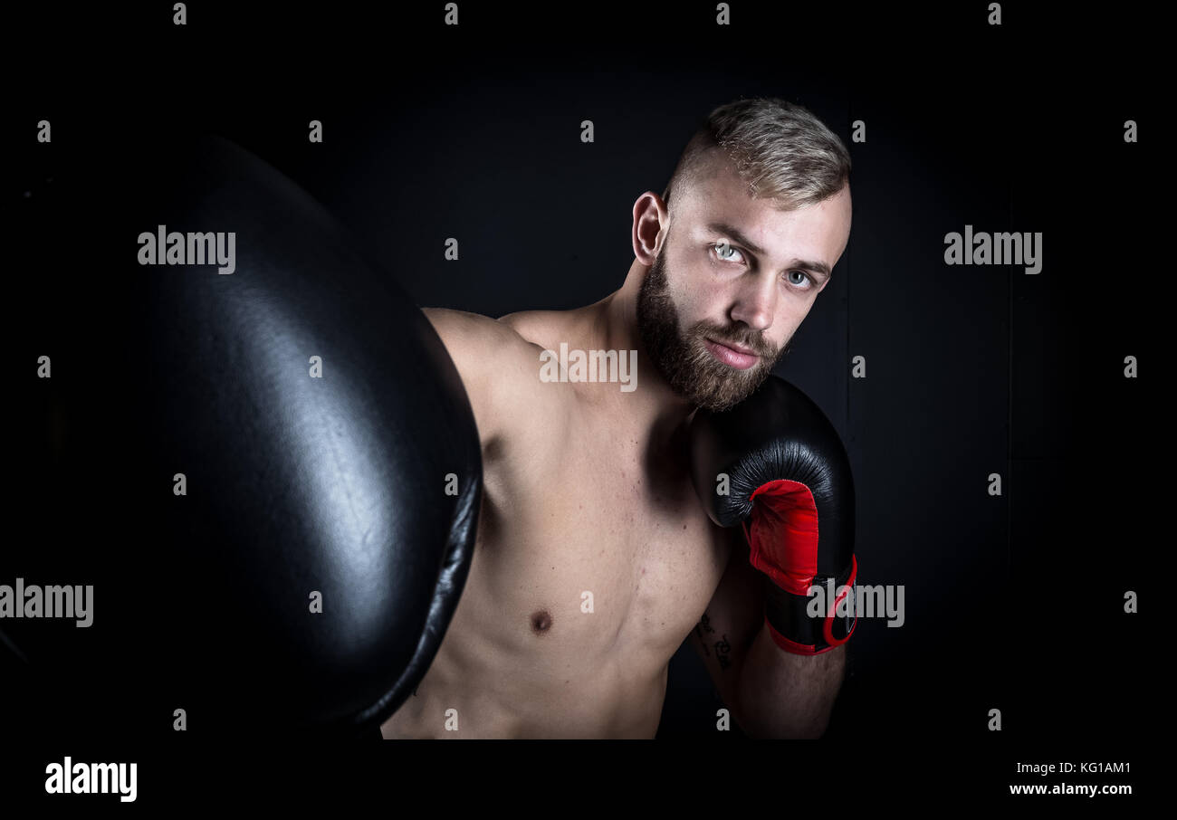 Male Athlete boxer punching a punching bag with dramatic edgy lighty in ...