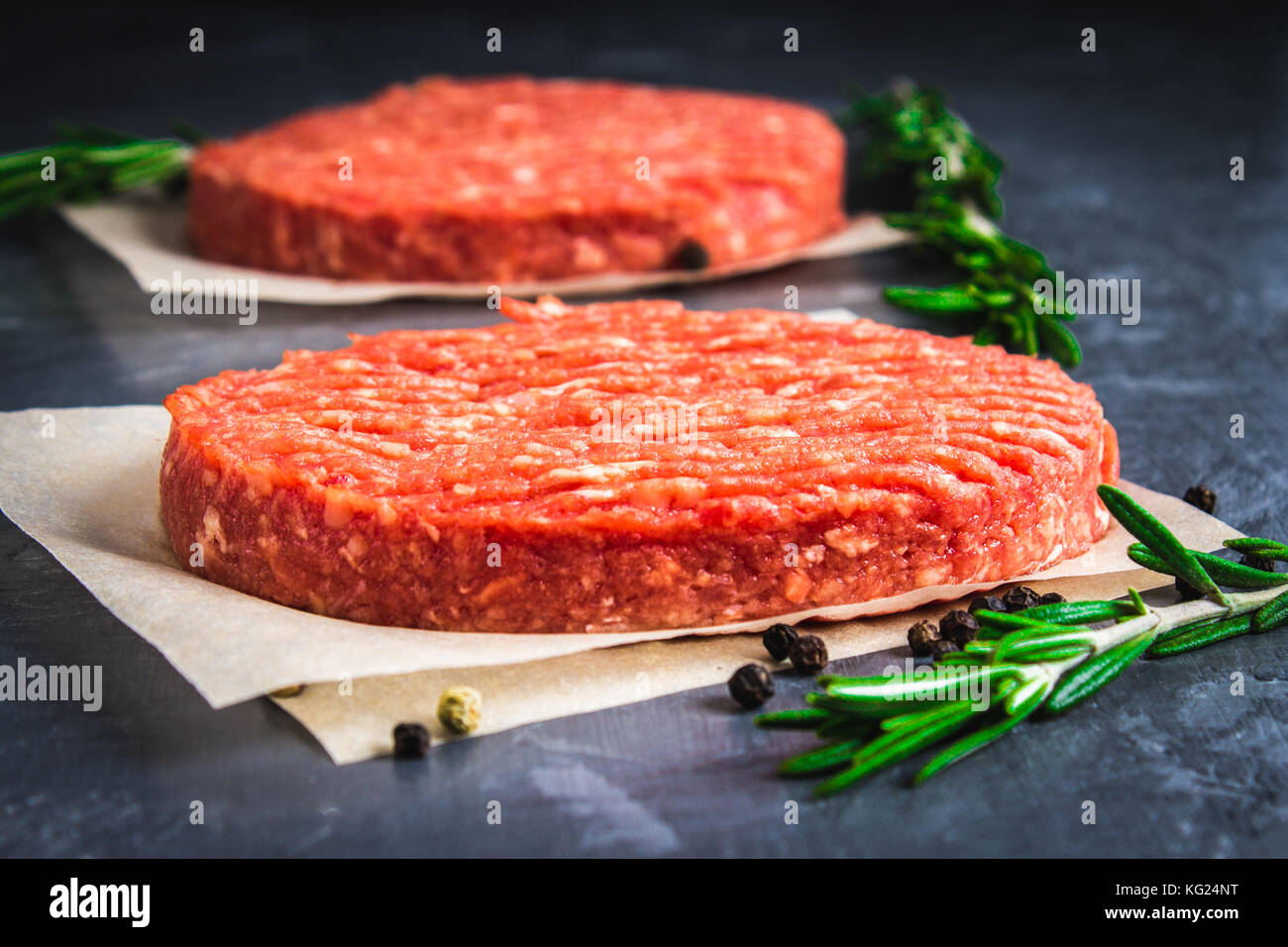 Raw burgers on parchment paper with rosemary. Grey marble background ...