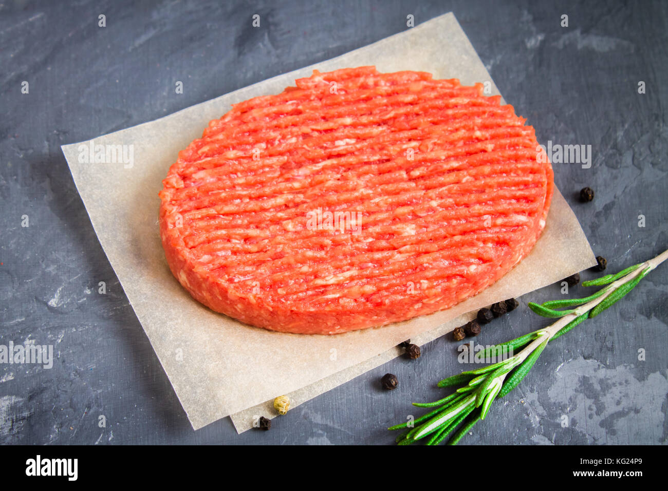 Raw burgers on parchment paper with rosemary. Grey marble background ...