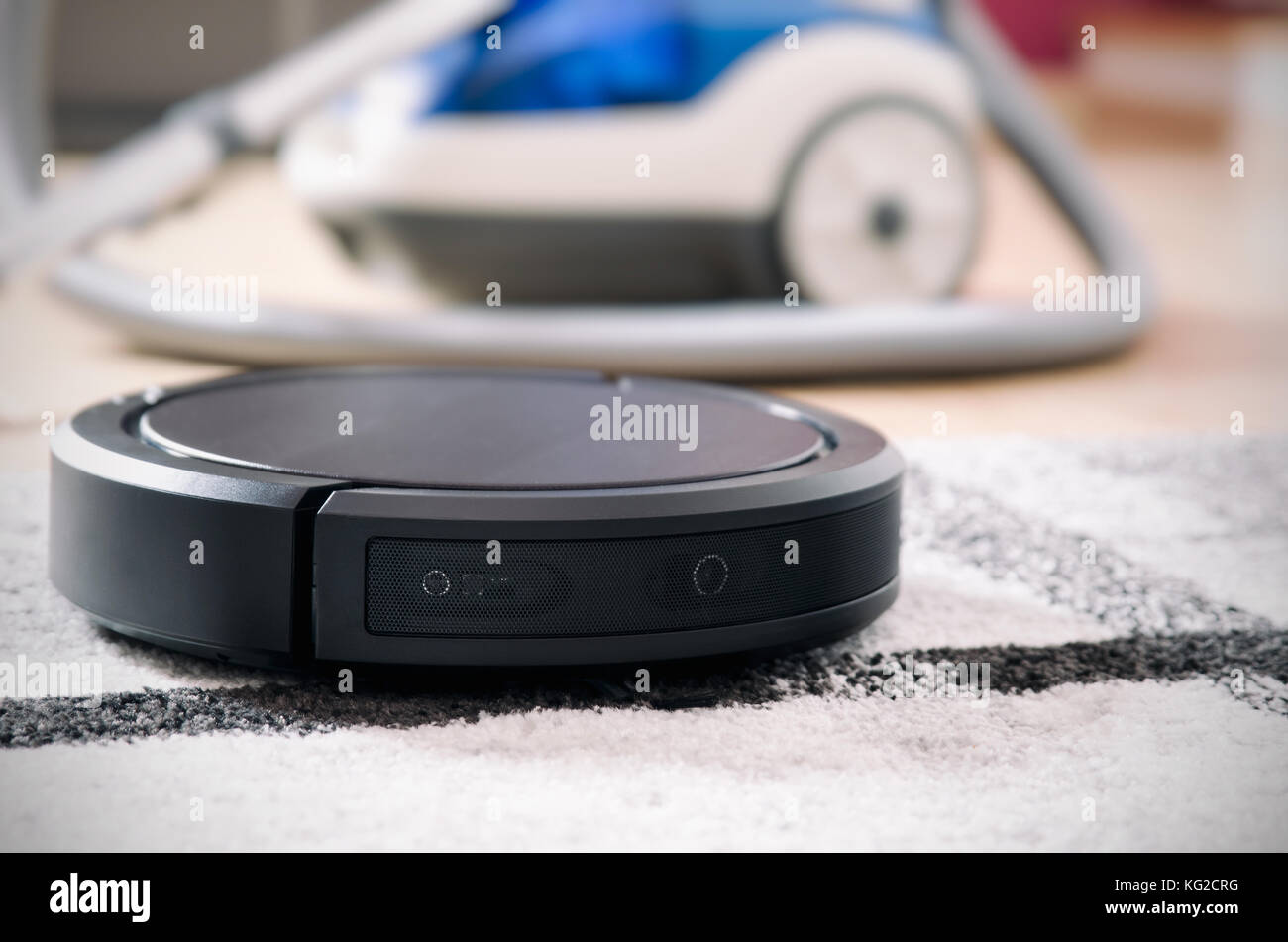 Robotic vacuum cleaner working on carpet. Traditional vacuum cleaner in ...