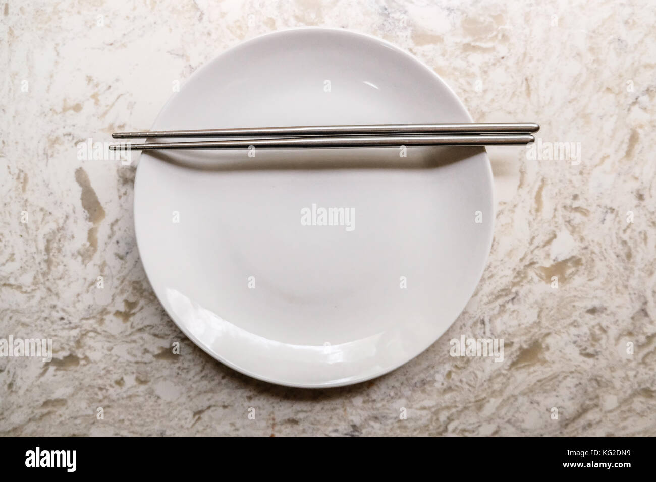 An empty white plate on a kitchen counter top with a pair of chopsticks ...