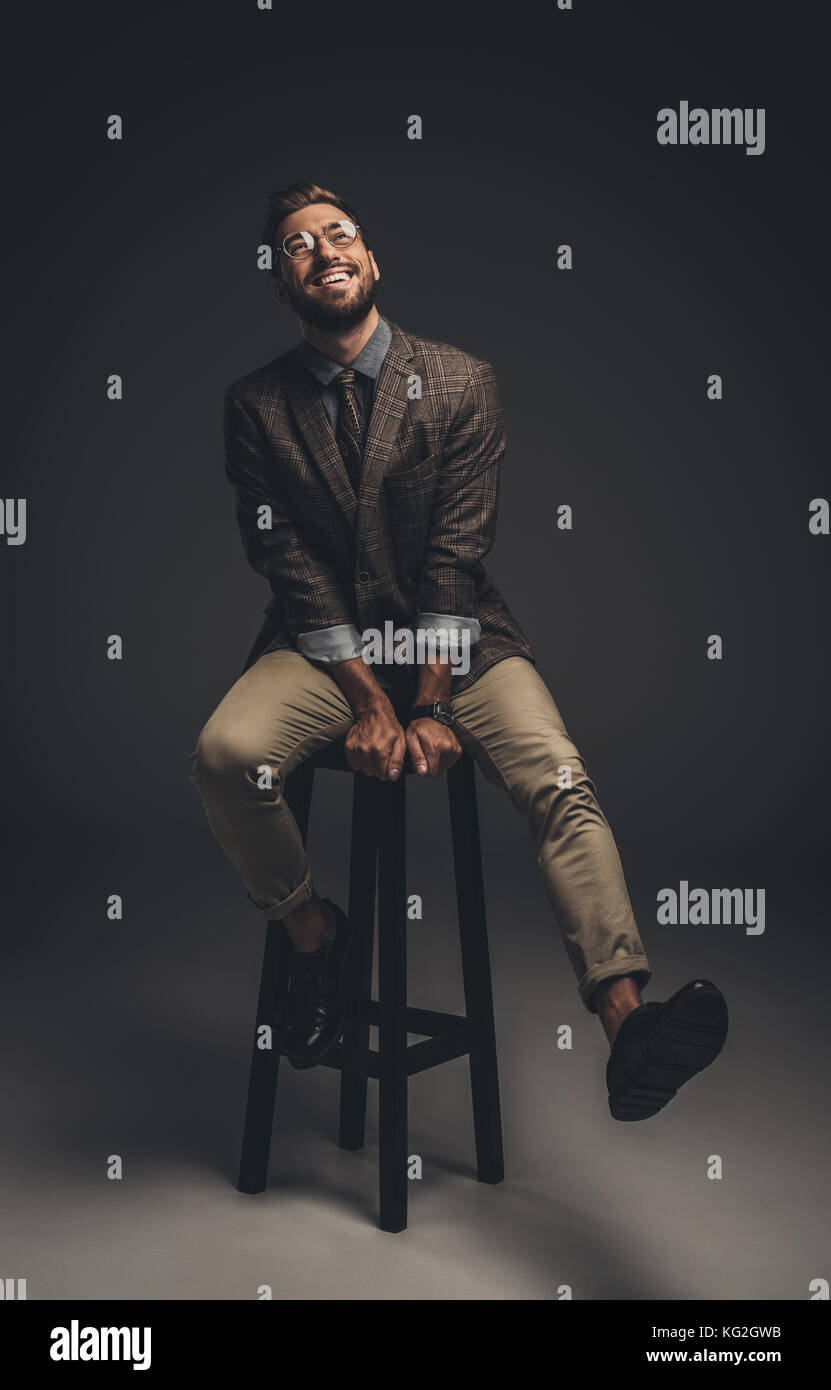 Laughing man in suit sitting on stool Stock Photo - Alamy