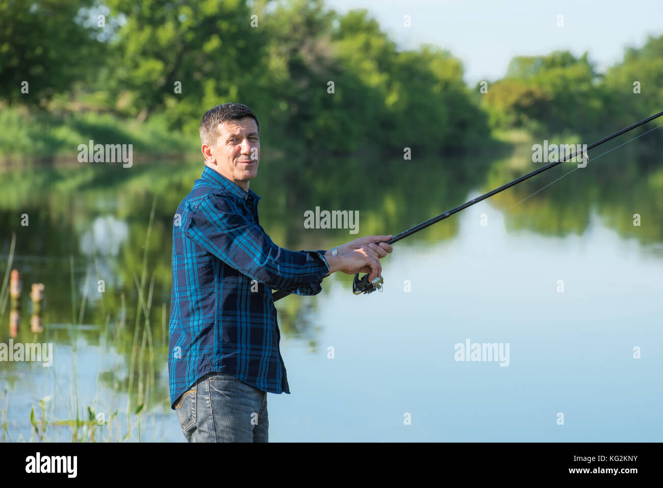 Sceptically smiling hobby fisherman with rod. Unfocused calm river at ...