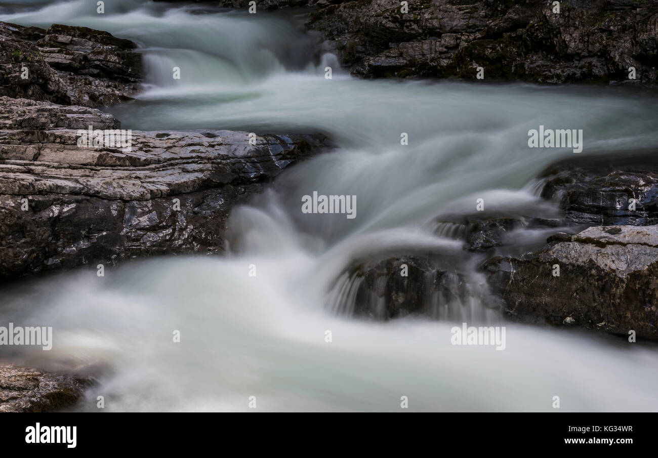 Fast flowing water in a creek with brown rocks and sunlight in Montafon ...