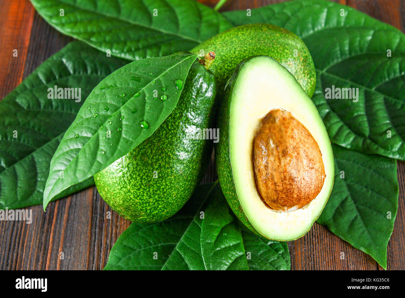 Three green raw ripe avocado fruits and a cut half with a bone with ...