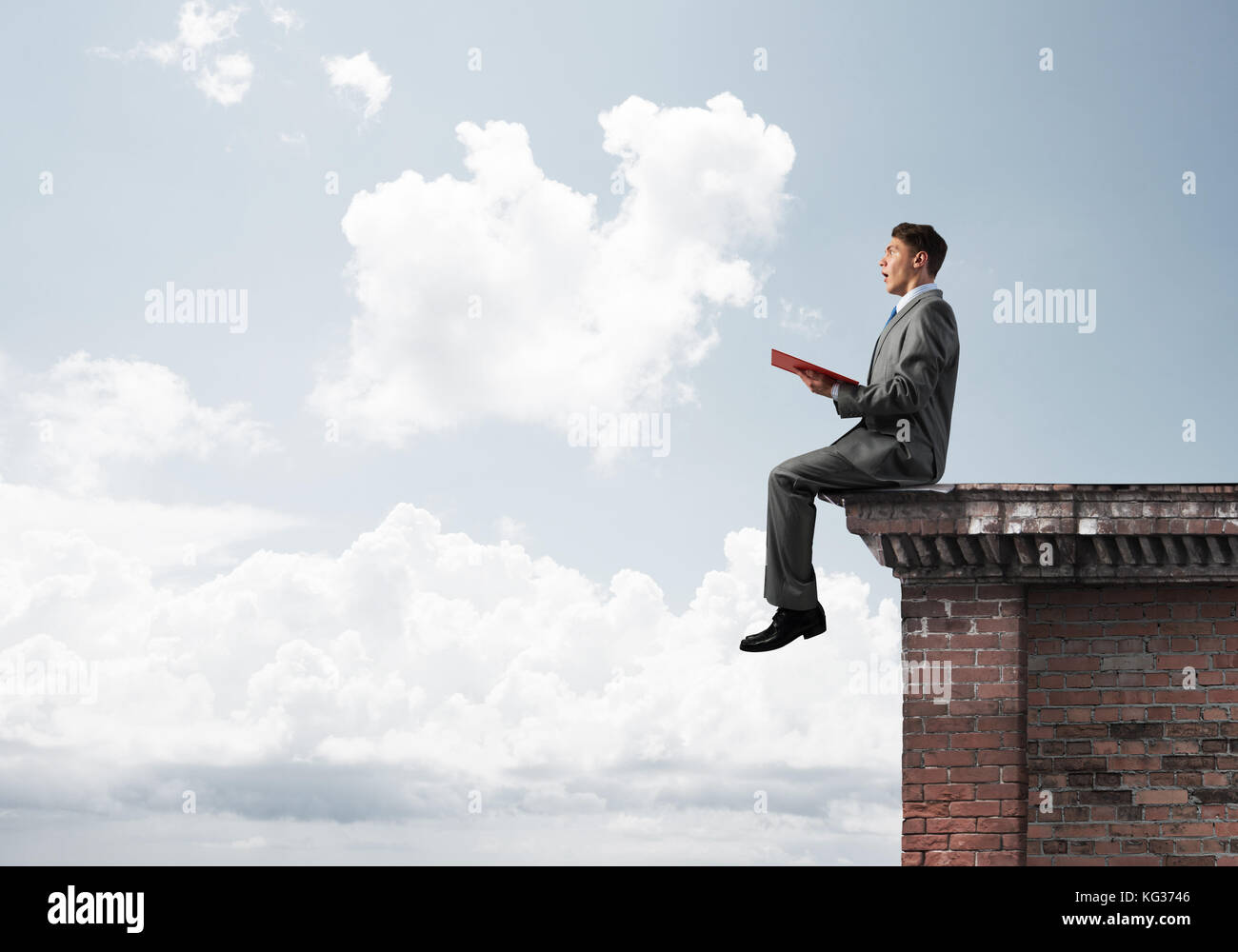 Man on roof edge reading book and cloudscape at background Stock Photo ...