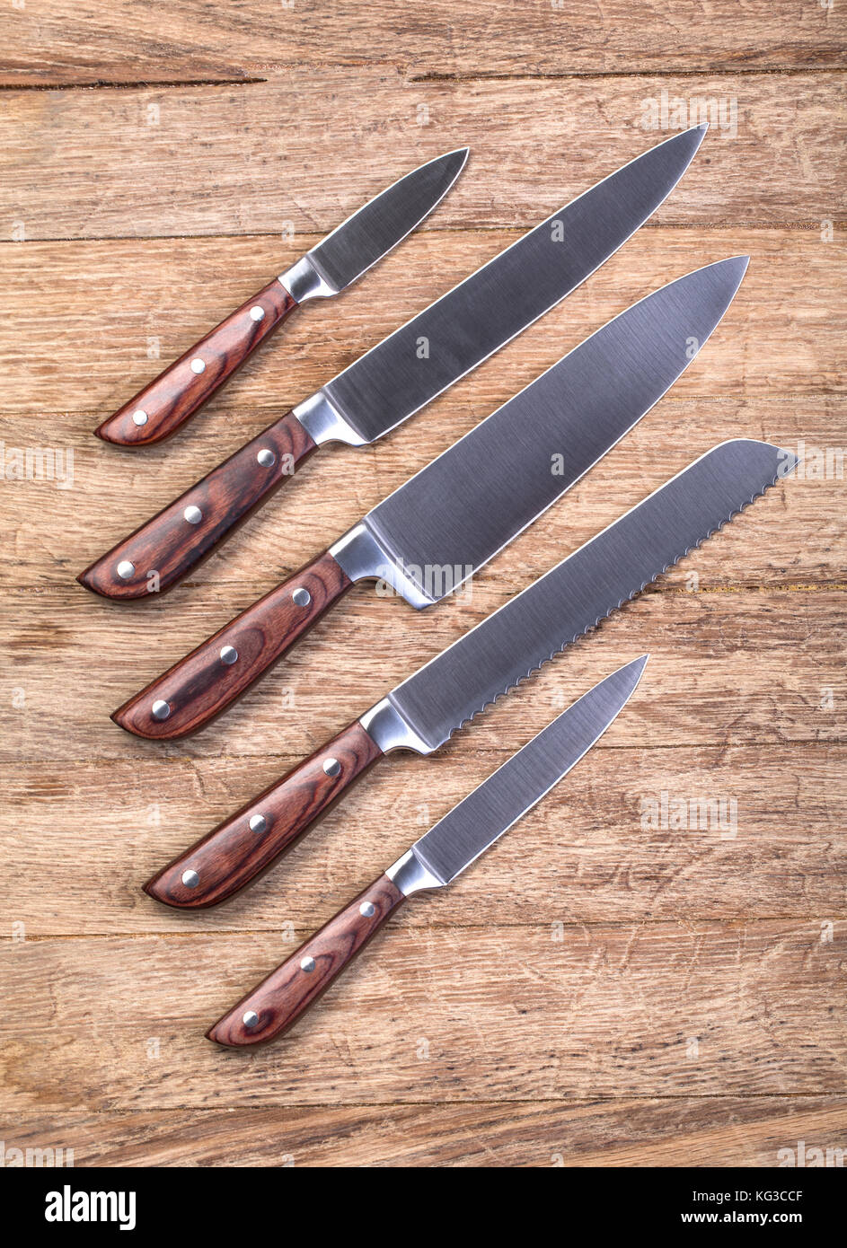 five kitchen knifes over brown wooden table Stock Photo - Alamy