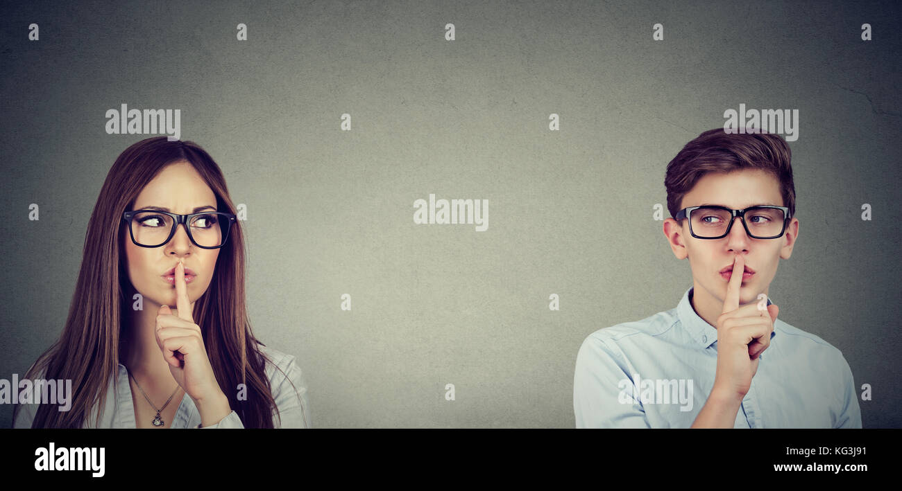 Secretive people. Young woman and man looking at each other saying hush ...