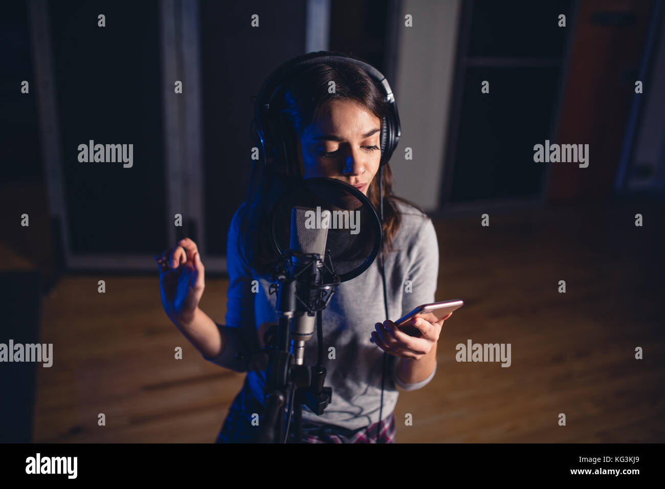 Young woman singing song with microphone and reading lyrics from mobile ...