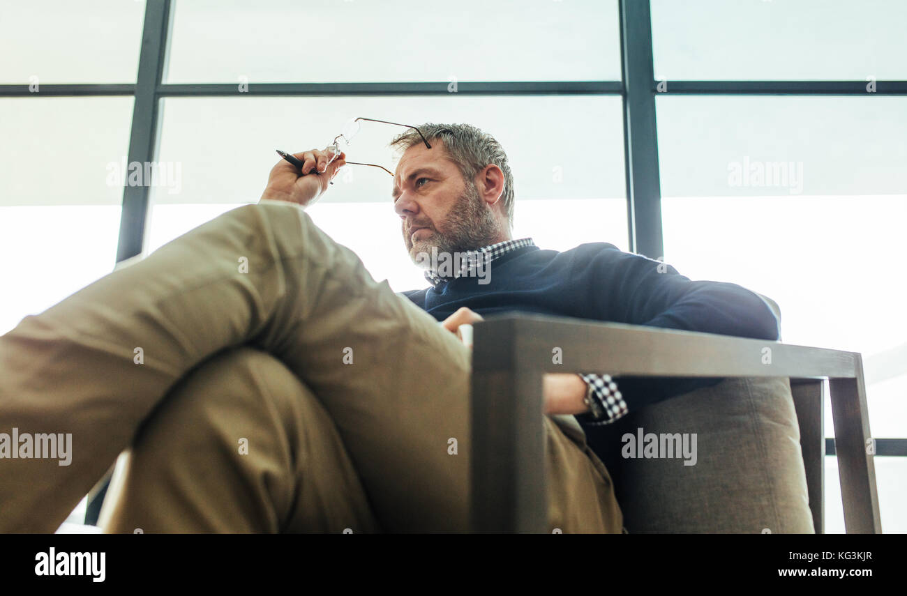 Psychotherapist with glasses sitting on arm chair in his office ...