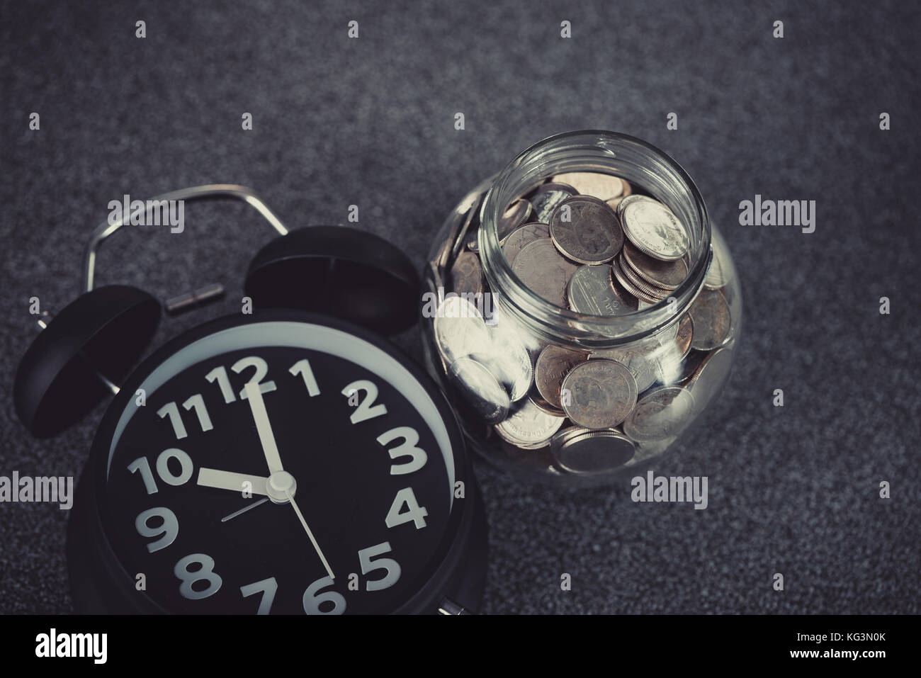 Alarm clock and step of coins stacks with coin in glass jar on working ...