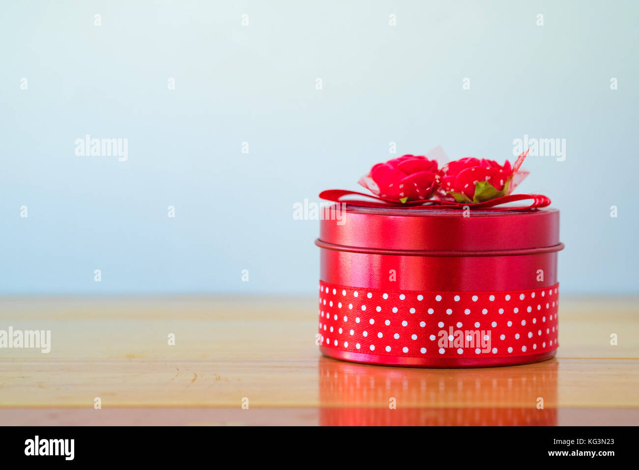 Round red gift box with ribbon bow on bright wooden table with copy ...