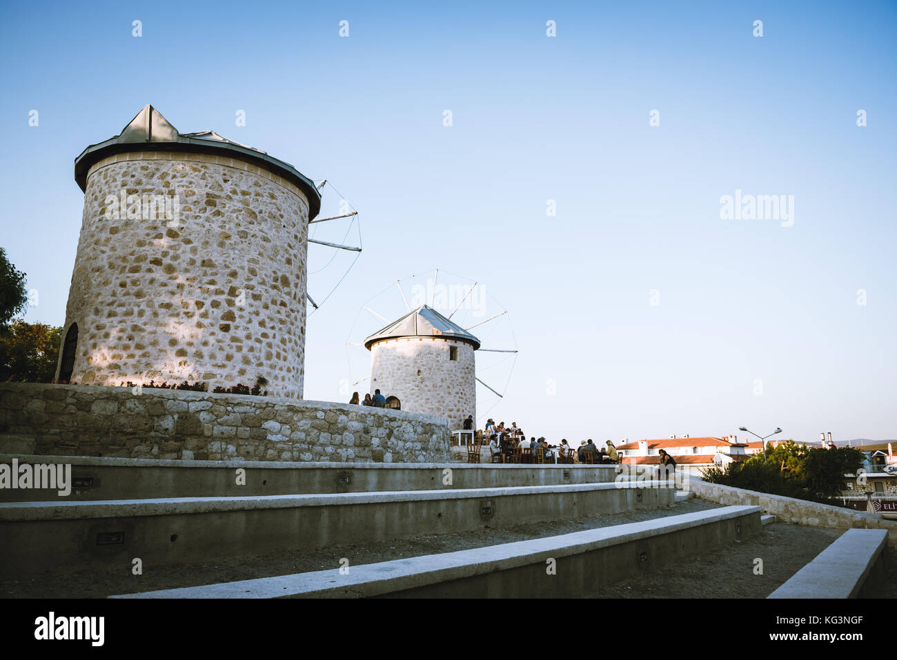 People visit ancient old stone windmills on a sunny day in Alacati town ...