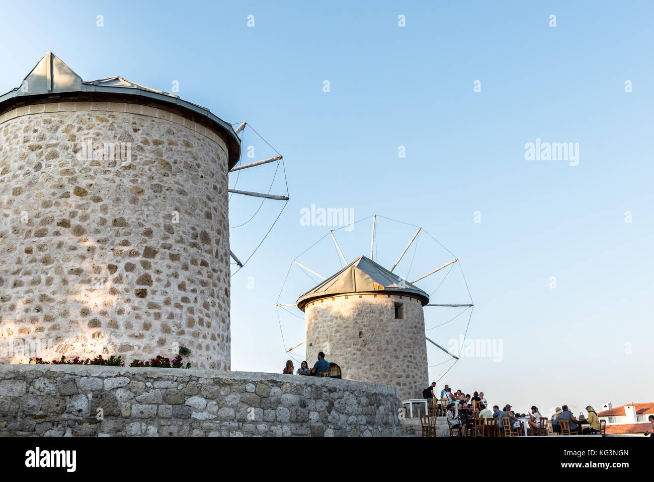 People visit ancient old stone windmills on a sunny day in Alacati town ...