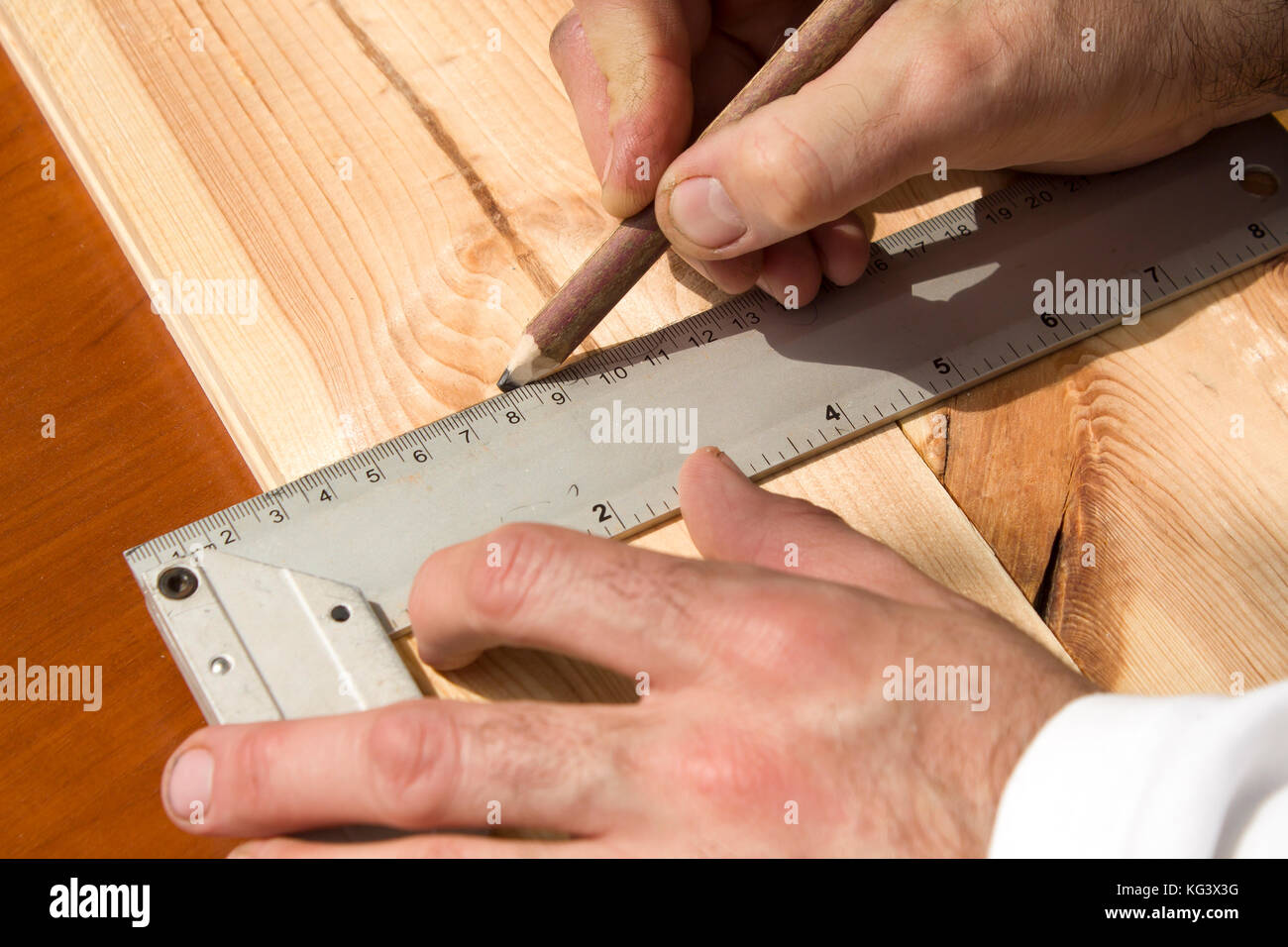 The carpenter's hands indicate the dimension on the board with a pencil ...