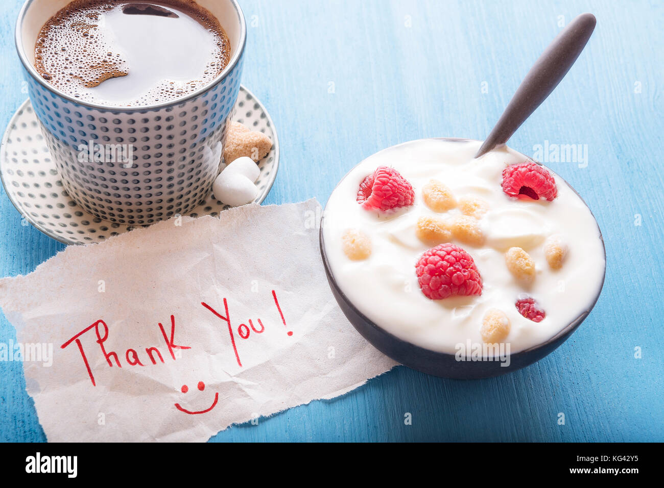 Bowl with yogurt, raspberry and cereal, a cup of hot coffee and a thank ...