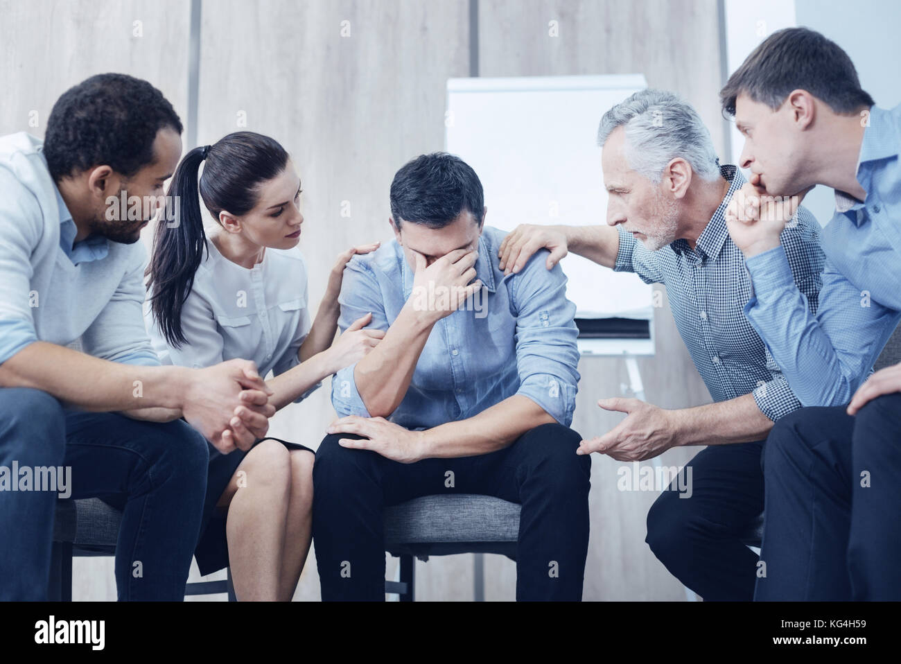 Serious colleagues sitting around their friend Stock Photo - Alamy