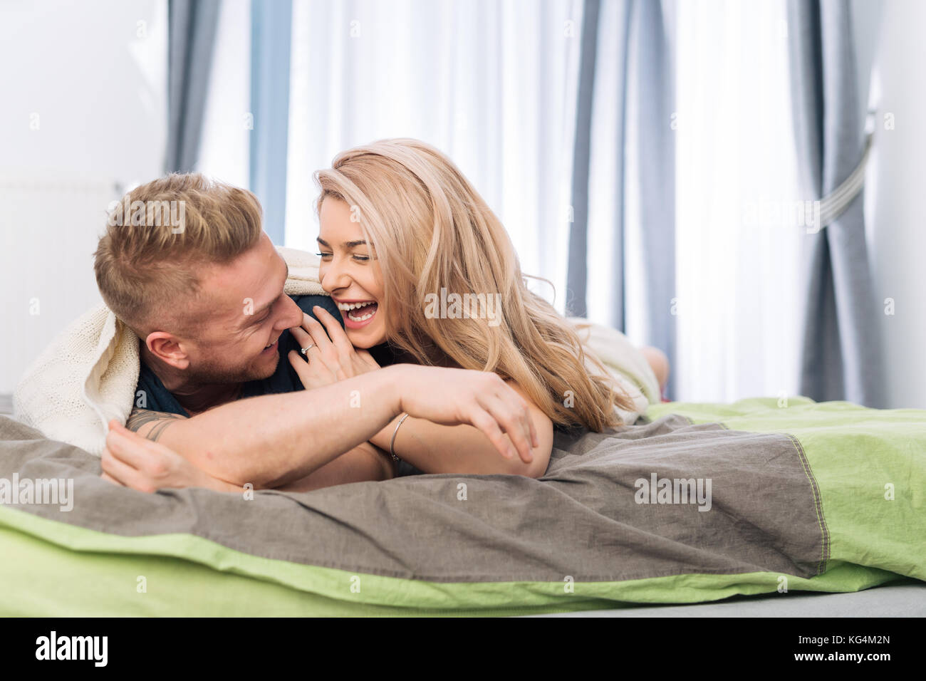 Happy cozy couple enjoying a good time in bed covered in a blanket ...