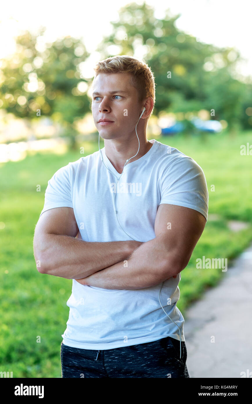 The man atlen stands in park with headphones, a white T-shirt. Summer ...