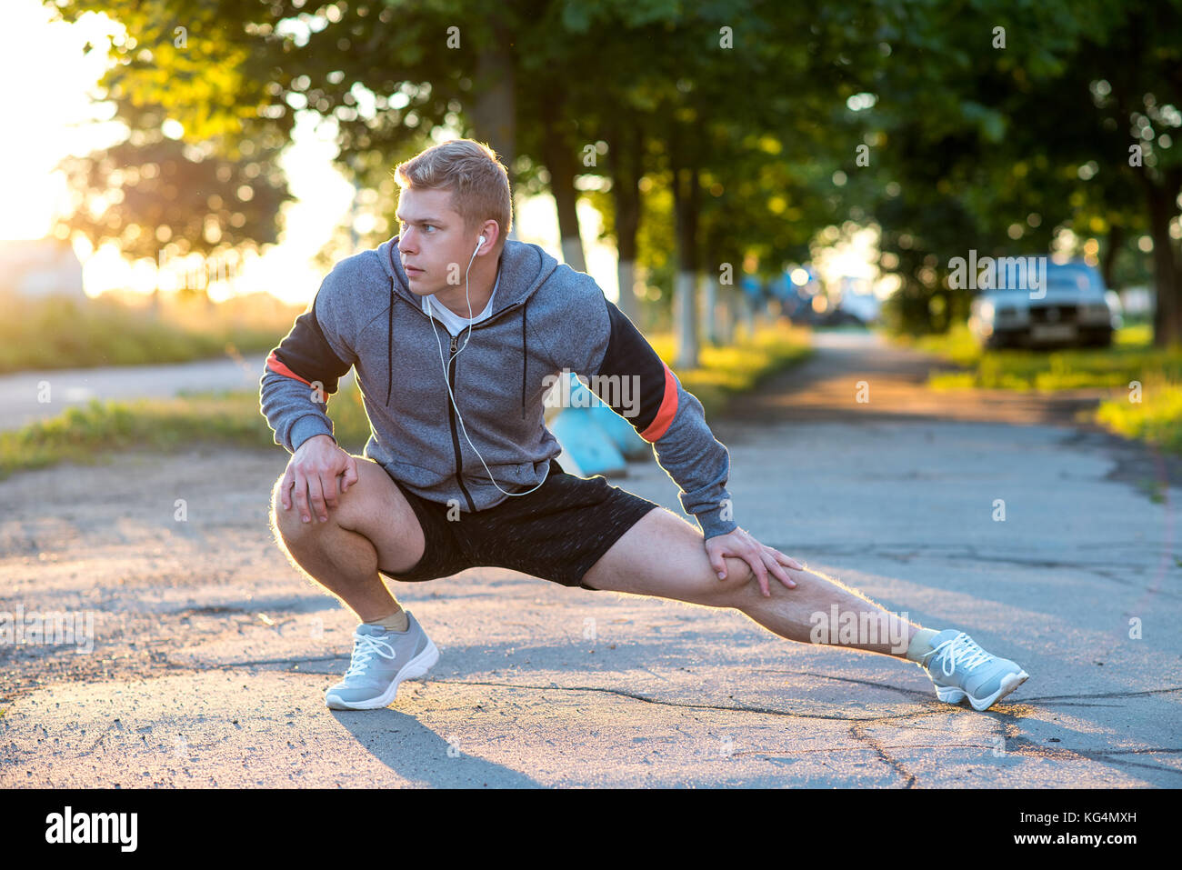 A young guy runner early morning makes gymnastics feet headphones. A ...