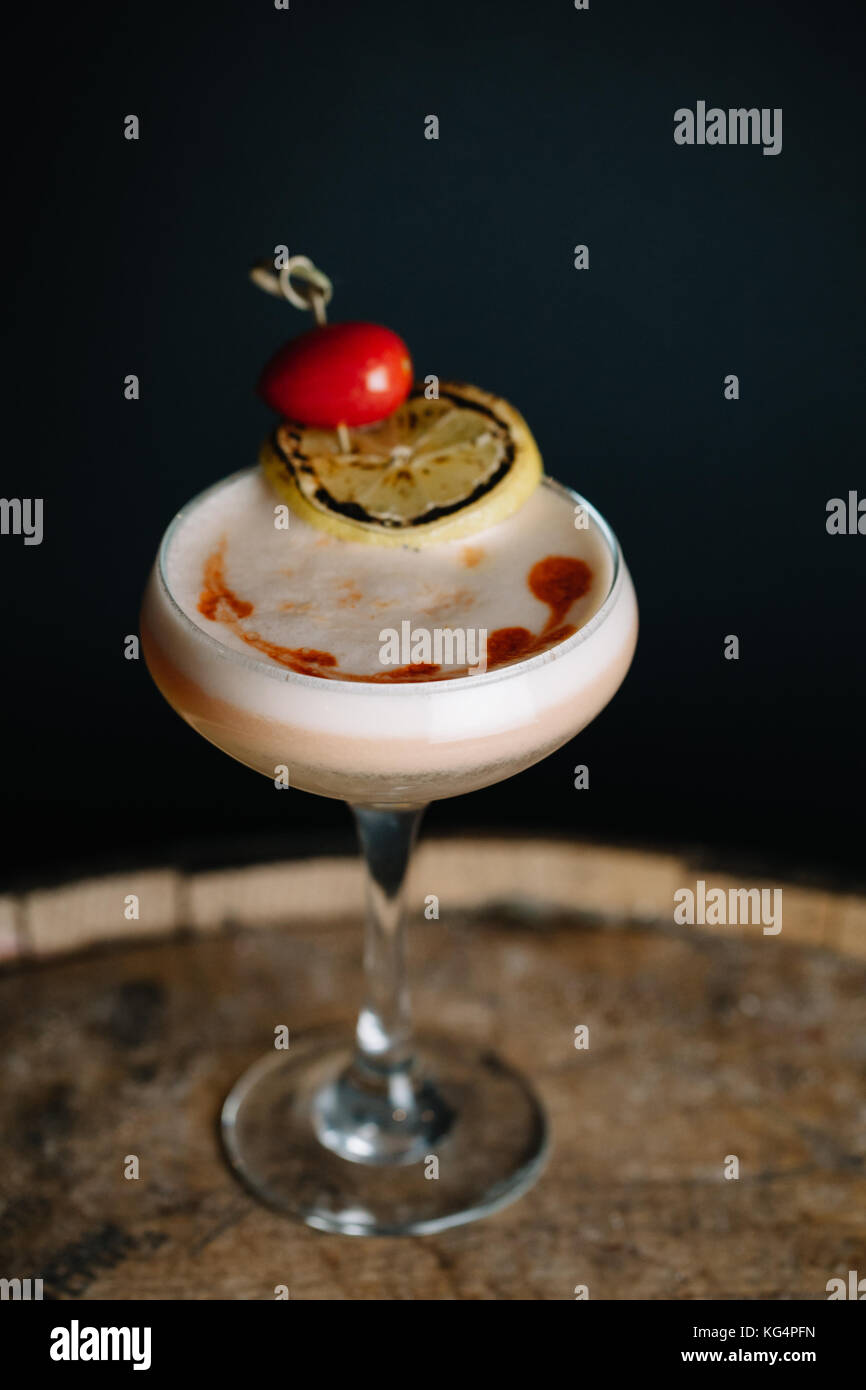 An alcoholic cocktail with egg foam garnished with a grape tomato and a ...