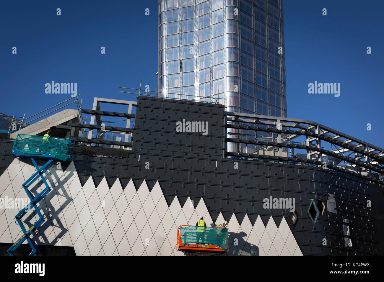 Workmen fix triangular-shaped cladding to the exterior of a part of the ...