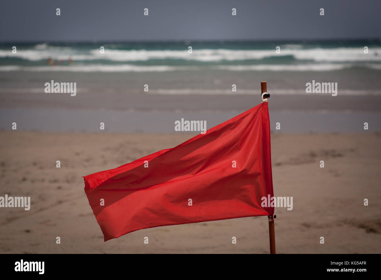 red flag flap on the beach, surfers in background Stock Photo - Alamy