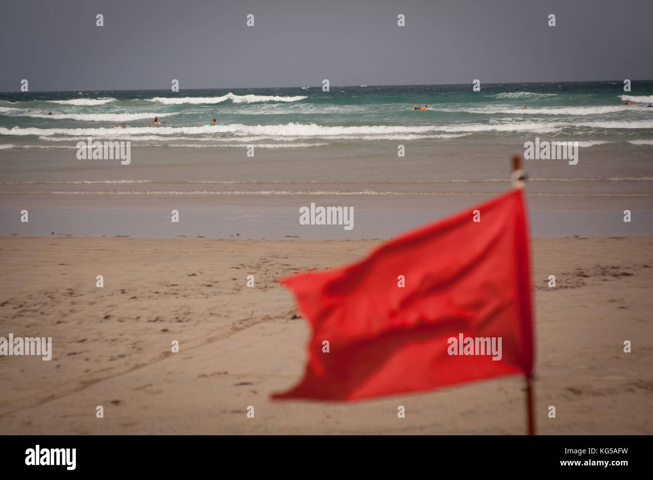 red flag flap on the beach, surfers in background Stock Photo - Alamy